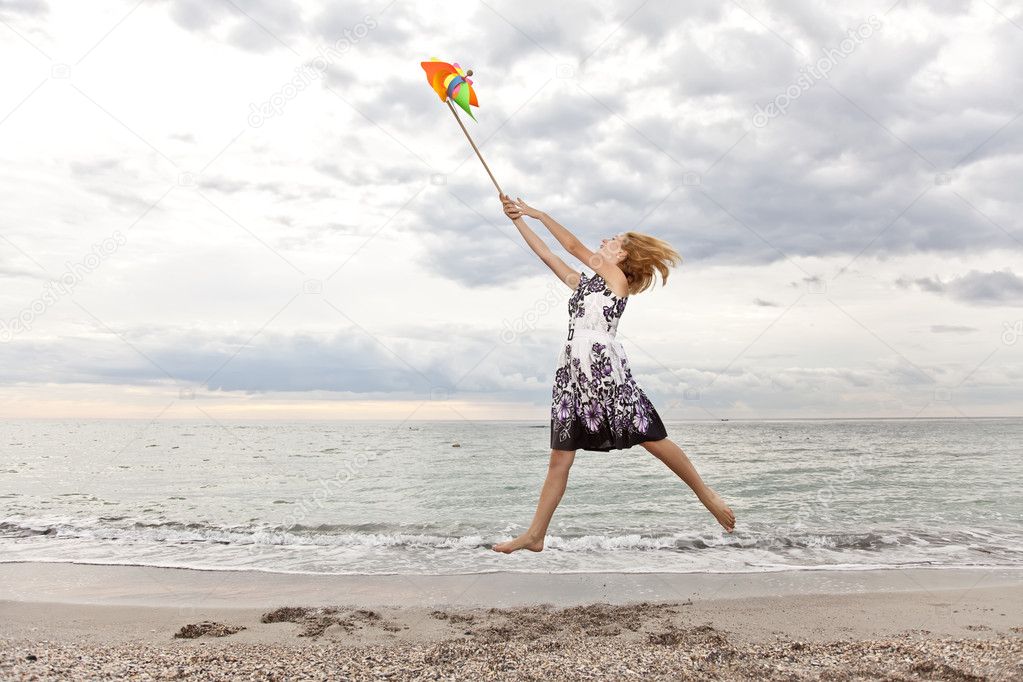Blonde girl jumping with wind turbine at beach. Stock Photo by ...